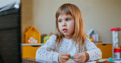 어린 소녀는 실내에서 노트북으로 온라인 학습 수업을 보고 다채로운 점토를 성형합니다 원격 가정 학습 개념입니다 사진