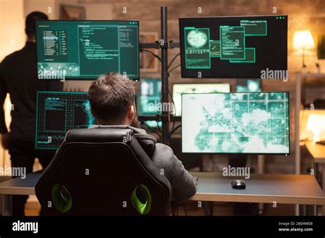 Rear View Of Hacker In Front Of Computer With Multiple Screens In Dark