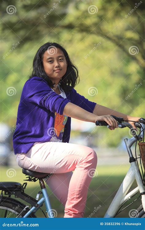 Asian Girl Riding Bicycle In Public Park With Green Blurry Background
