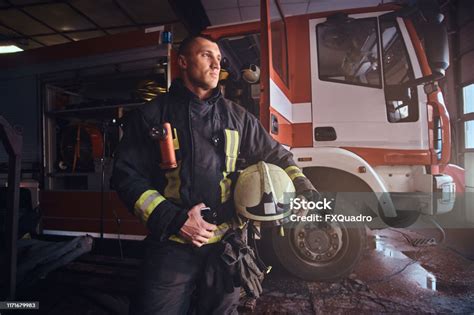 제복을 입은 소방관이 소방서 차고에서 소방차 근처에 서있는 동안 밖을 바라보고 있습니다 소방관에 대한 스톡 사진 및 기타 이미지 소방관 소방차 구명 기구 Istock