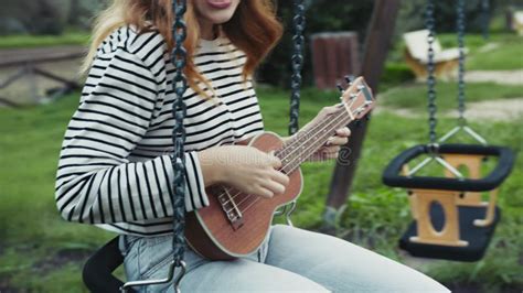 Young Woman Practices Playing The Ukulele Seated In A Swing Stock Video