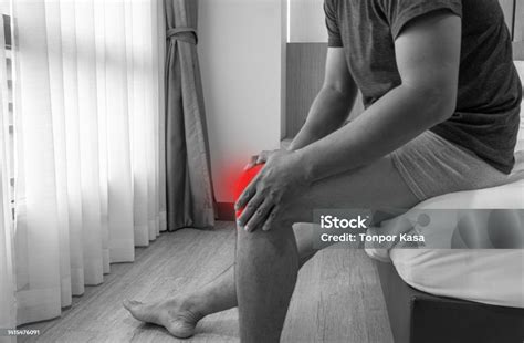 남자의 무릎과 다리 통증을 닫고 젊은 남자는 통증 염증 증상으로 무릎을 잡고 침대 의료 의료 개념에 앉아 있습니다 가정의 방에