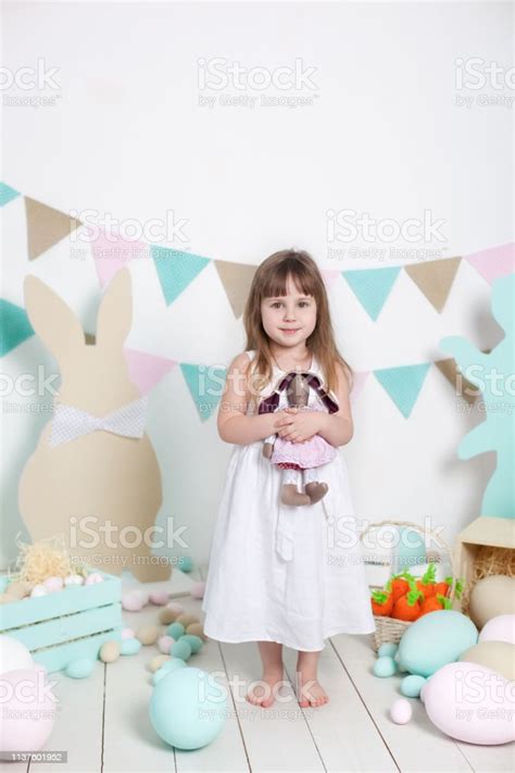 부활절 하얀 드레스에 아름 다운 어린 소녀는 부활절 토끼를 포옹 하 고 있습니다 많은 다른 화려한 부활절 달걀 화려한 인테리어