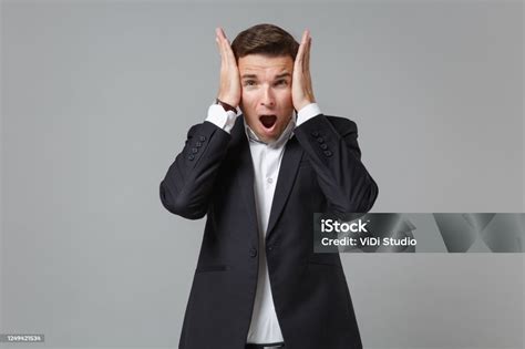 회색 벽 배경에 고립 된 포즈 고전적인 검은 정장 셔츠에 젊은 사업가 를 충격 성취 경력 재산 사업 개념 복사 공간을 모의합니다