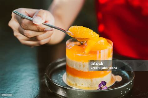 오렌지 조각과 크림을 곁들인 맛있는 레이어 디저트로 유리잔에 담겨 제공됩니다 사람은 생생한 색상과 질감을 보여주는 이 달콤한 간식을 즐기고 있습니다 0명에 대한 스톡 사진