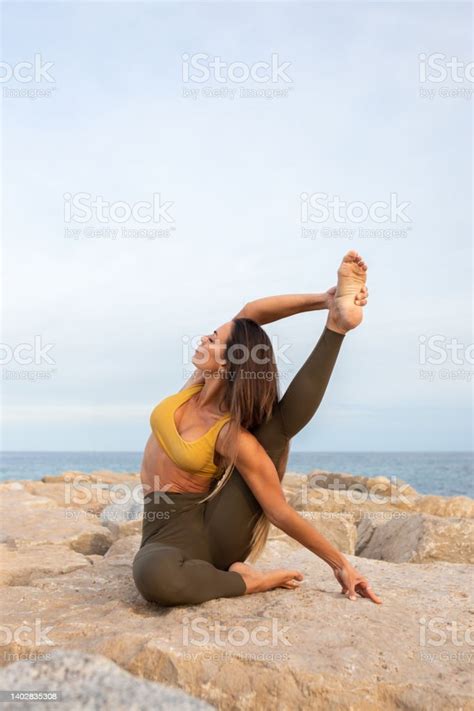 Parivritta Kraunchasana 요가를하는 유연한 젊은 여성은 바다 근처의 바위에 포즈를 취합니다 공간을 복사합니다 세로 이미지 바다에 대한 스톡 사진 및 기타