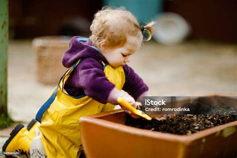 봄 날에 모래와 삽을 가지고 노는 귀여운 사랑스러운 유아 소녀 노란 부츠와 진흙 비 웅덩이 바지를 입은 아기 아이 봄에 야채를 심는 행복한 소녀 놀이에 대한 스톡 사진 및
