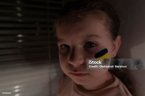 뺨에 우크라이나 국기가 그려진 소녀는 블라인드가있는 창문 근처의 어두운 방에 서 있습니다 6 7 살에 대한 스톡 사진 및 기타 이미지 6 7 살 가정의 방 개념