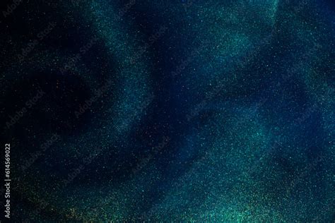 A Sparkling Swirl Of Gold Particles In Blue Liquid With Green Hues