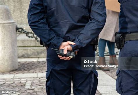 파란색 유니폼을 입은 익명의 경찰관이 무전기 라디오를 들고 손을 클로즈업하고 팔을 뒤로 하고 있었다 통신 경찰 순찰 개념 근무에