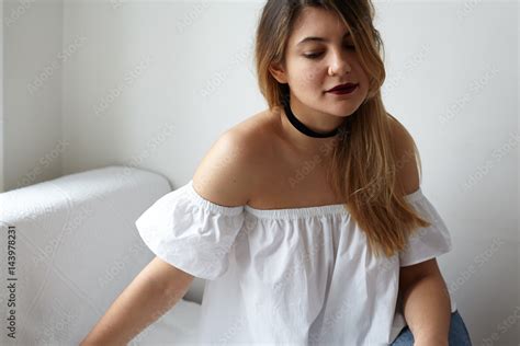 Attractive Young Woman In White Blouse With Poen Shoulders Looking Down