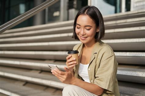 Une Fille Urbaine Heureuse Boit Son Café à Emporter Et Fait Défiler Ses