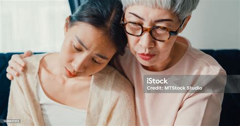 아시아 은퇴 시니어 어머니는 소파 소파에 앉아 집에서 슬픔에 빠진 십대 딸에게 위로의 따뜻한 포옹을 안겨줍니다 노인에 대한 스톡