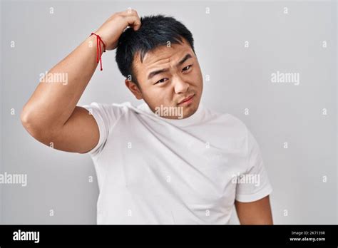 Young Chinese Man Standing Over White Background Confuse And Wondering About Question Uncertain