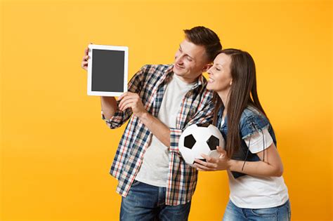 젊은 커플 팬 여자 사람 지원 팀을 응원 하는 축구 팬 들 재미 있는 노란색 배경에 고립 된 축구 공을 빈 검은색 빈 화면으로 태블릿 Pc 컴퓨터를 들고 스포츠 가족 라이프
