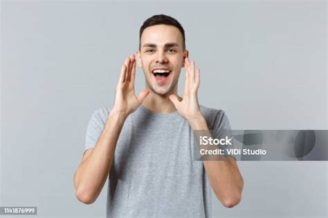 캐주얼에서 쾌활 한 젊은 남자의 초상화 스튜디오에서 회색 벽 배경에 고립 된 입 근처 손 제스처와 비명 사람들은 진심으로 감정 라이프 스타일 개념입니다 복사 공간을 모의