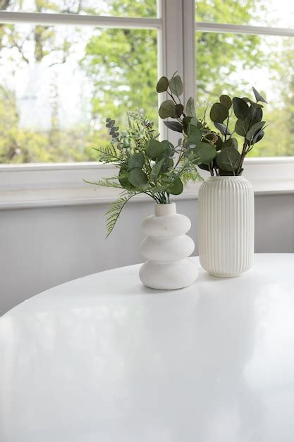 Fondo de dos jarrones blancos con vegetación artificial en una mesa