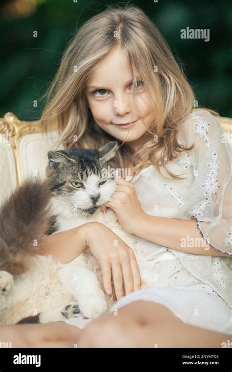 Little Blond Girl In White Dress Cuddling Her Cat Sitting On Cream And