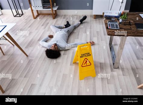 Mature Man Falling On Wet Floor In Front Of Caution Sign At Office