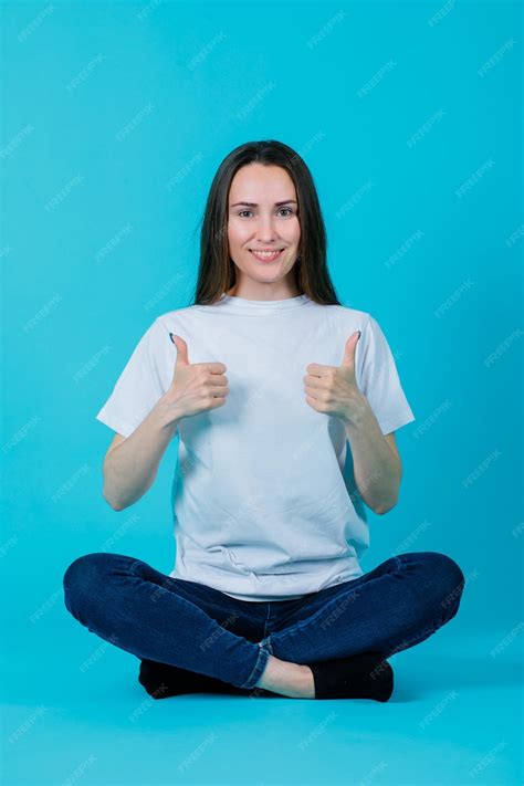 A Jovem Sorridente Está Mostrando Gestos Perfeitos Sentando Se No Chão Sobre Fundo Azul Foto