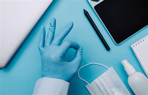 파란색 의료 수술 보호 장갑의 손은 노트북 그래픽 태블릿 의료 마스크 선명한 파란색 배경에 스프레이의 배경에 Ok 기호를 보여줍니다 코로노바이러스 검역 모드의 홈 오피스