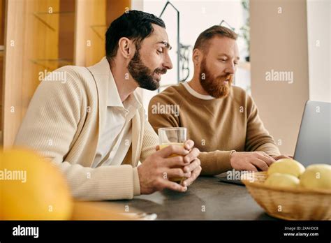 A Happy Gay Couple Is Seated At A Table Focused On A Laptop Screen In