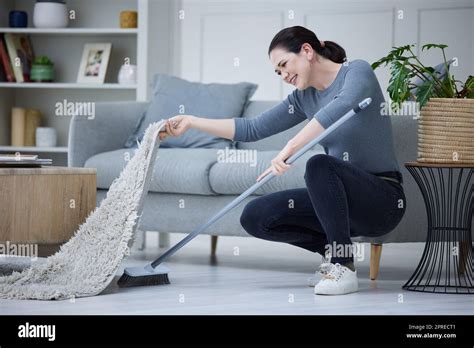Woman Cleaning Home And With Broom Sweeping Carpet For Daily Chores