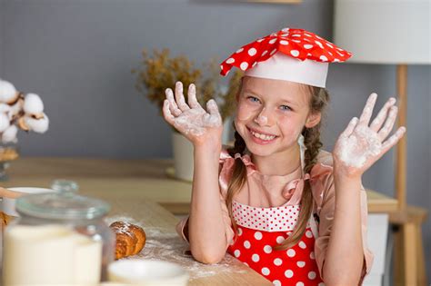 빨간 물방울 무늬 앞치마와 모자를 쓴 소녀가 부엌에서 요리합니다 아이들의 영양과 교육 부엌에 있는 아이들 아이들을위한 요리법 아이는 부엌에서 음식을 준비합니다 아동 보호