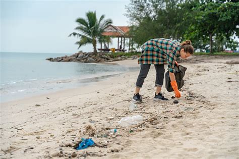 환경 오염과 바다의 문제 오렌지 장갑을 입은 젊은 여성은 열대 해변의 검은 쓰레기 봉투에 플라스틱과 쓰레기를 청소합니다 따기에 대한 스톡 사진 및 기타 이미지 Istock