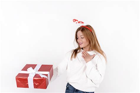 흰색 스웨터를 입고 크리스마스 선물 상자를 들고 재미있는 머리 후프를 입고 흰색 배경에 고립 된 아름다운 젊은 여성 12월에