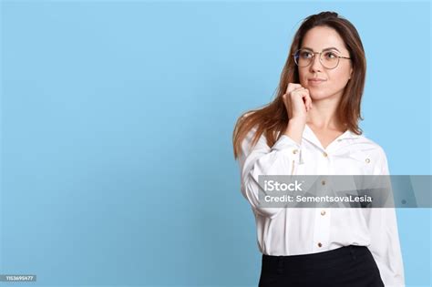 그녀의 턱을 만지고 젊은 잠겨있는 여자의 초상화 마음에 뭔가가 파란색 배경 위에 고립 된 흰색 셔츠와 검은 치마를 입고 사려