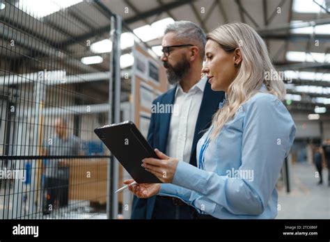 Female Engineer And Male Production Manager Standing In Modern Industrial Factory Talking About