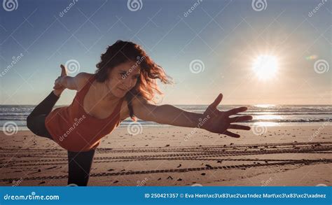 Adult Woman In Yoga Pose On The Beach At Dawn With The Sun Rising From