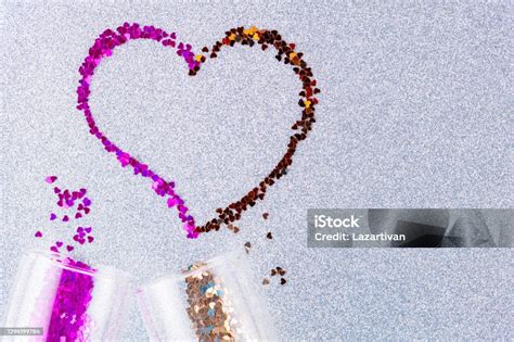 여러 가지 빛깔의 반짝이로 만든 하트 모양 궁극의 회색 반짝이 배경 위에 하트 모양의 색종이가 튀어나온 샴페인 안경 2장
