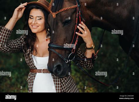 Pregnant Girl With A Big Belly In A Hat Next To Horses In The Forest In