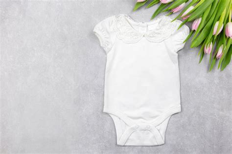 하얀 아기 소녀 보디 슈트 모형 플랫은 회색 콘크리트 배경에 분홍색 튤립 꽃으로 누워 있습니다 Oneie 템플릿 디자인 인쇄