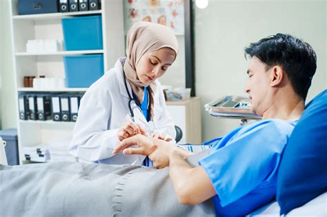 두 명의 무슬림 여성 의사가 병원에서 수술 후 침대에 누워 있는 남성 환자의 병력과 증상을 확인하고 회복 및 건강 상태를 모니터링합니다 2명에 대한 스톡 사진 및 기타