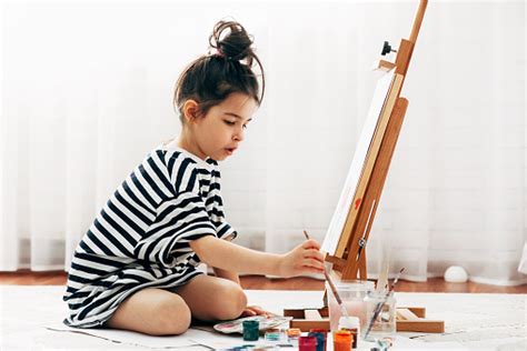 집에서 이젤에 종이에 페인트 브러시와 어린 소녀 미취학 아동 그림의 수평 전체 길이 이미지 잠그고 있는 동안 바닥에 앉아 방에