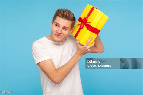 귀 근처에 생일 상자를 들고 흰색 티셔츠를 입은 청년 내부의 내용을 듣고 불신을 표현 20 29세에 대한 스톡 사진 및 기타 이미지 20 29세 T 셔츠 공휴일