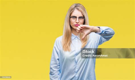 젊은 아름 다운 금발 비즈니스 우먼 불행 하 게 보이고 분노 하 고 제스처 아래로 엄지 손가락으로 부정적인 보여주는 고립 된 배경 위에 안경을 착용 잘못 된 식입니다 개념에