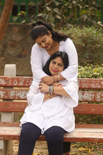 하얀 드레스를 입은 행복한 인도 어머니와 딸이 도시 공원의 벤치에 앉아 아름다운 순간을 보내고 있다 사랑하는 엄마와 사랑스러운 딸 2명에 대한 스톡 사진 및 기타 이미지
