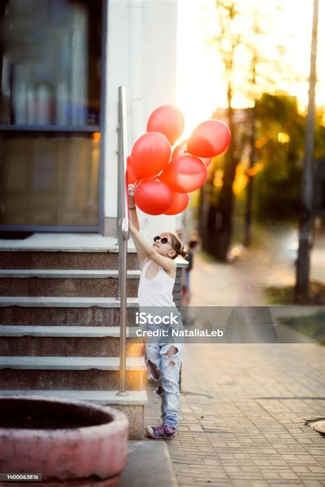 맑은 여름날 계단에 빨간 풍선이 달린 찢어진 청바지를 입은 유럽 어린이 십대 소녀 도시 거리의 일몰에 선글라스를 착용 한 어린이 Z 세대 생일 축하 8 9 살에 대한 스톡