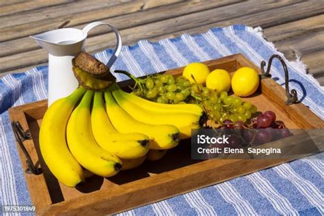 나무 쟁반에 다양한 종류의 신선한 익은 과일 바나나 포도 레몬 통하고 있는 푸른 식탁보 와 통하고 있는 화창한 날에 정물 사진입니다 선택적 초점 흐릿한 배경 0명에 대한