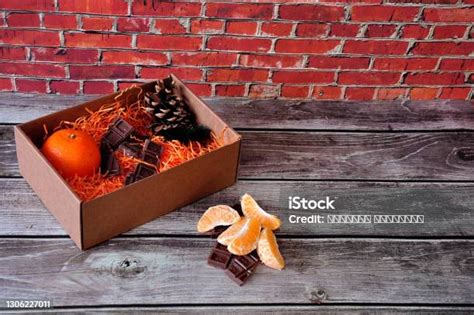 귤과 소나무 콘이 있는 골판지 상자는 초콜릿 웨지와 감귤류 조각 옆에 있는 나무 테이블에 놓여 있습니다 갈색에 대한 스톡 사진