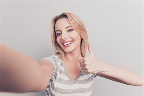 세련 된 예쁜 매력적인 여자의 손으로 Selfie 회색 배경에 고립 된 스마트 폰의 전면 카메라 촬영 기호를 엄지를 보여주는