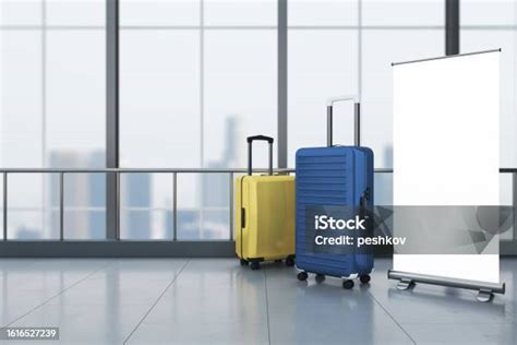 텅 빈 흰색 포스터에 로고나 텍스트를 넣을 수 있는 공간이 있는 빈 흰색 포스터의 투시도는 여행 가방 옆에 있는 빈 공항 복도 홀에 큰 창문에서 도시 전망을 배경으로 합니다