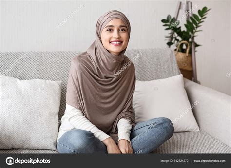Beautiful Girl In Hijab Sitting On Couch And Smiling To Camera Stock