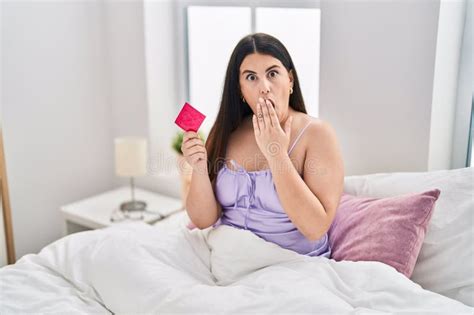 Young Brunette Woman Wearing Lingerie And Holding Condom On The Bed