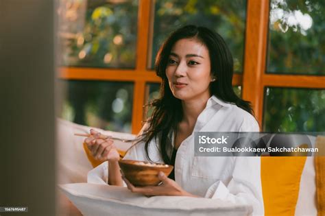 건강한 음식을 먹는 여성 집 거실의 소파 베드에서 과일과 요구르트를 곁들인 건강한 아침 식사를 하는 젊은 아시아 여성 20 29세에 대한 스톡 사진 및 기타 이미지 Istock