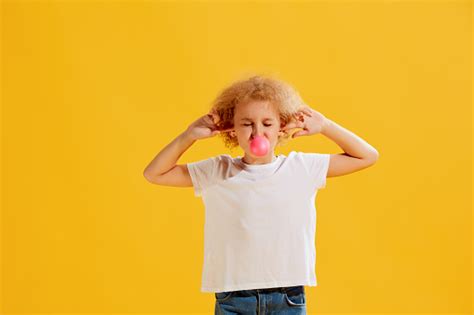 행복하고 평온한 어린 시절 학령기 소녀 노란색 배경 위에 고립 된 껌 거품을 불어 넣는 아이 어린이 감정의 개념 6 7 살에